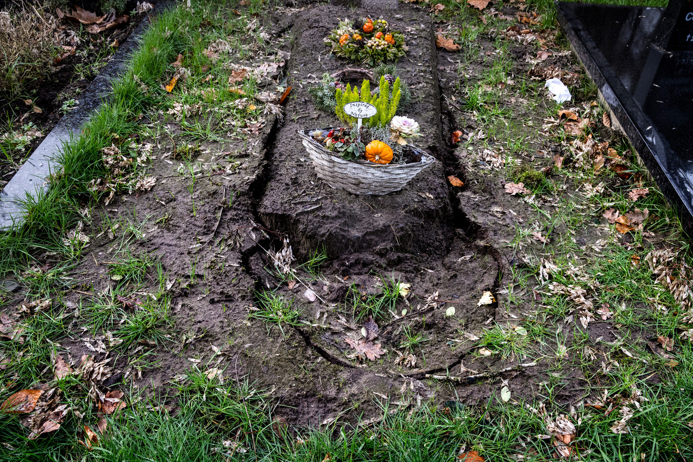 Regen spoelt veel zand weg op begraafplaatsen, bezoekers kijken naar ...